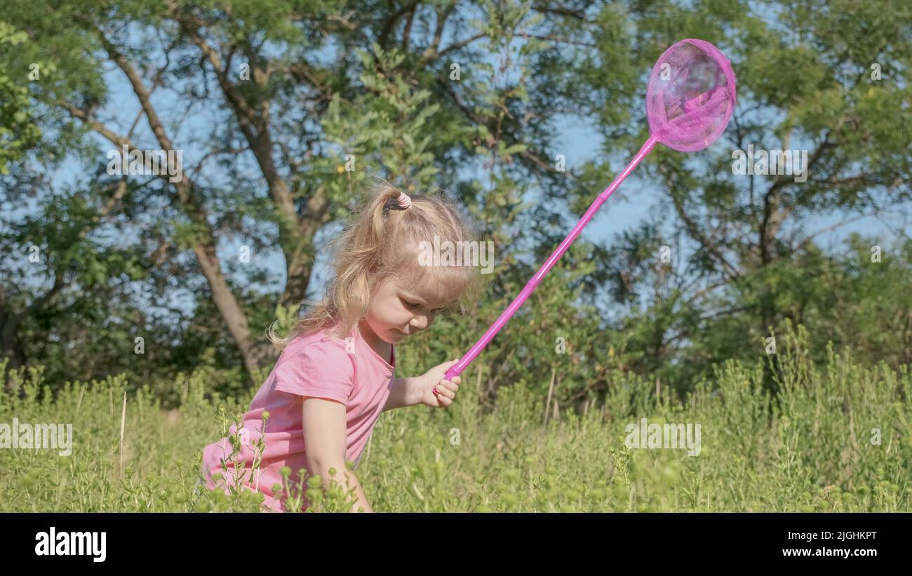 Little girl plays with butterfly net of tall grass in city park. Cute ...