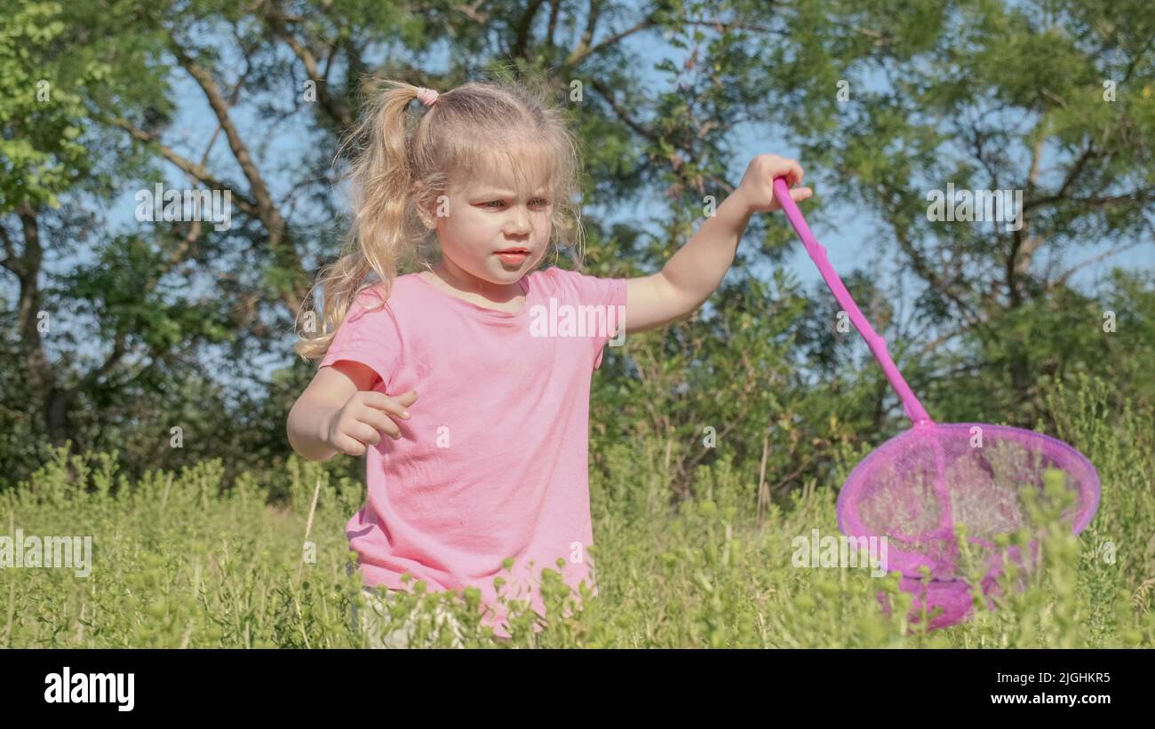 Little girl plays with butterfly net of tall grass in city park. Cute ...