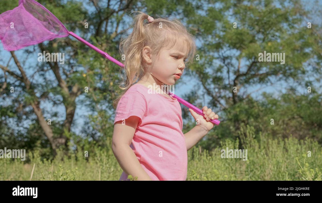 Little girl plays with butterfly net of tall grass in city park. Cute ...