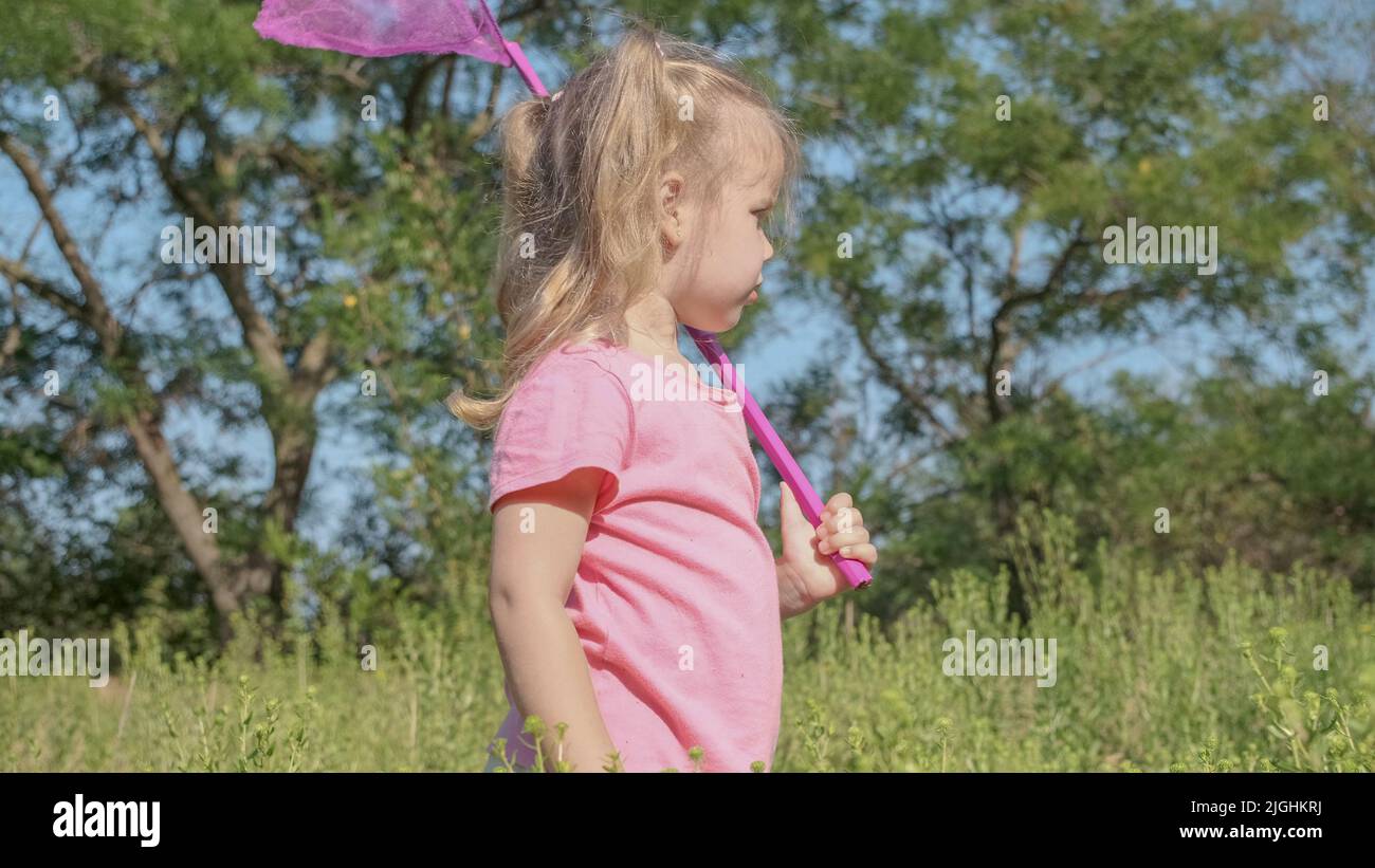 Little girl plays with butterfly net of tall grass in city park. Cute ...