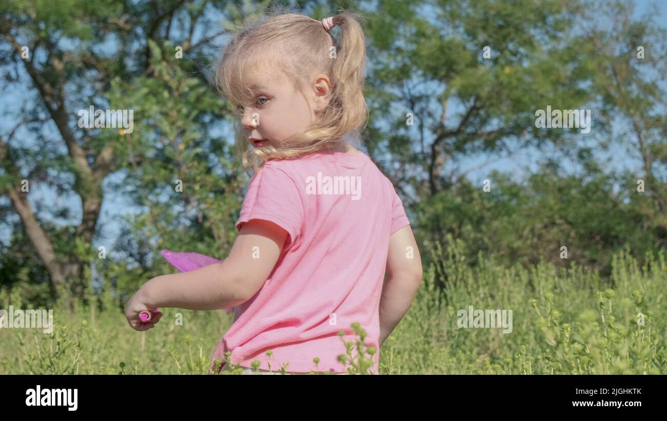 Little girl plays with butterfly net of tall grass in city park. Cute ...
