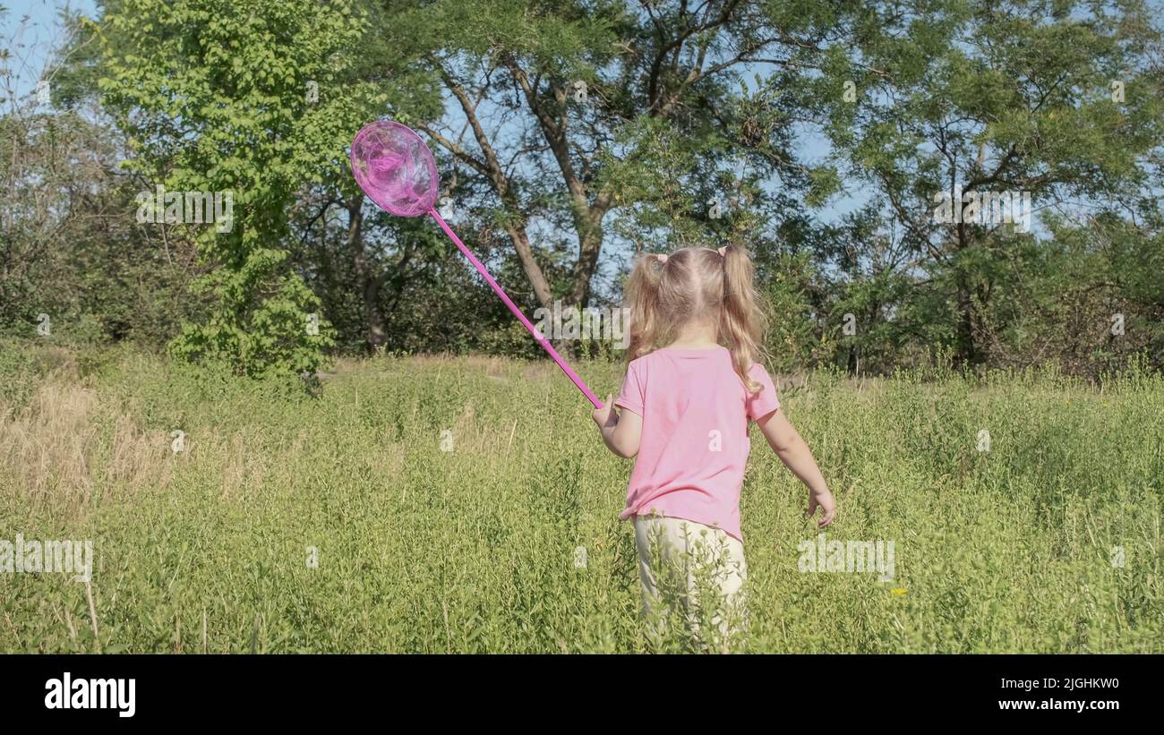 Little girl plays with butterfly net of tall grass in city park. Cute ...