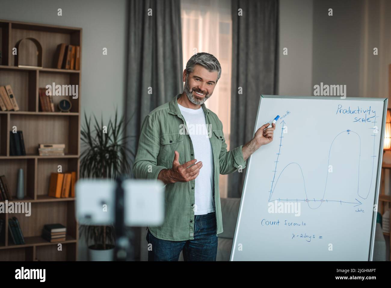 Glad caucasian senior man teacher tutor with beard looks at smartphone ...