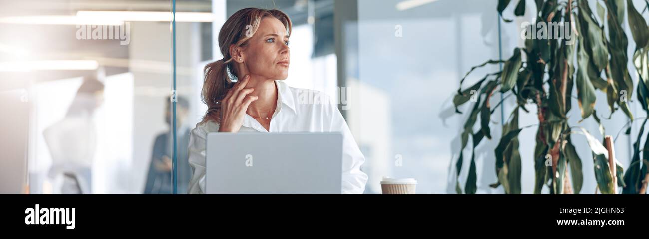 Focused businesswoman working on laptop and looking out the window at ...