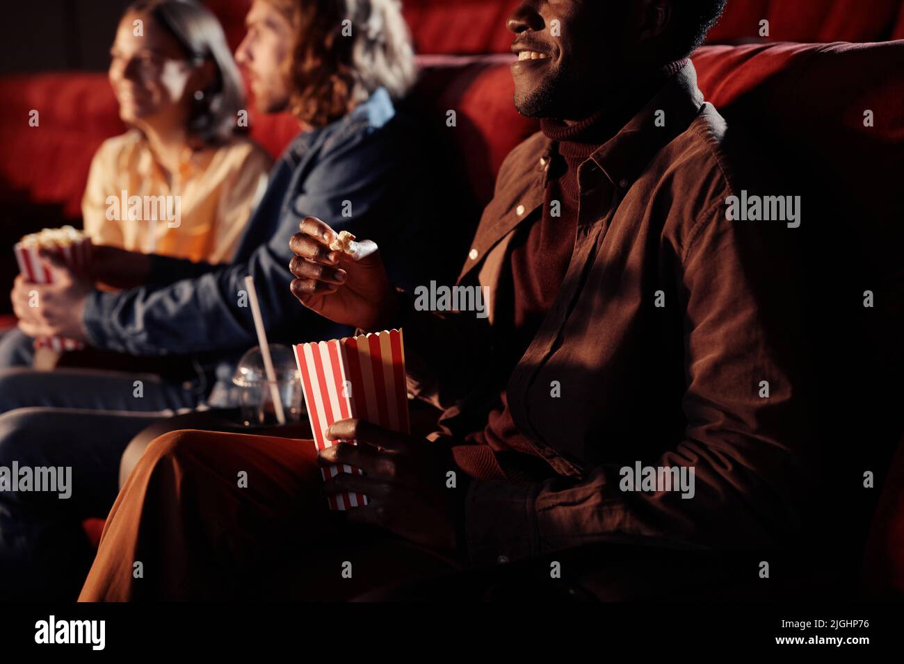 African young man eating popcorn and watching movie together with his ...