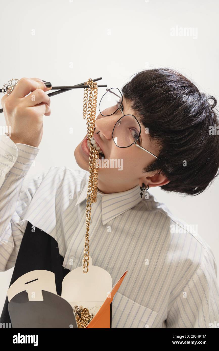 Portrait of stylish young man eating golden necklaces like noodles ...