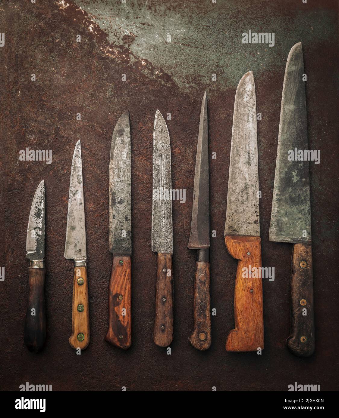 flat lay of various carbon steel knives with wooden handle on old rusty ...