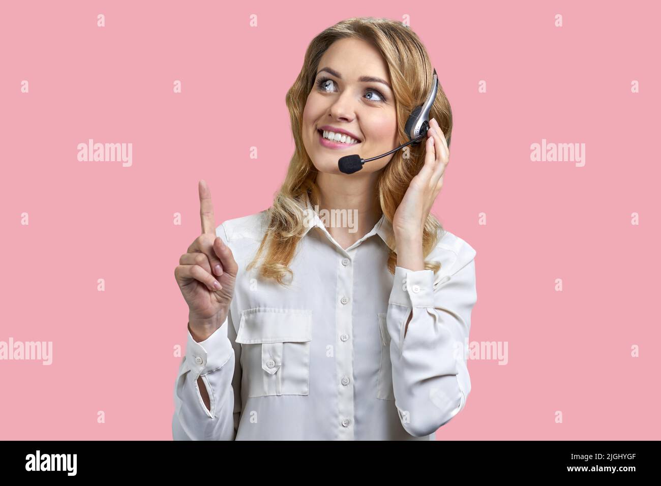 Female phone operator in headset pointing with finger upwards on pink ...