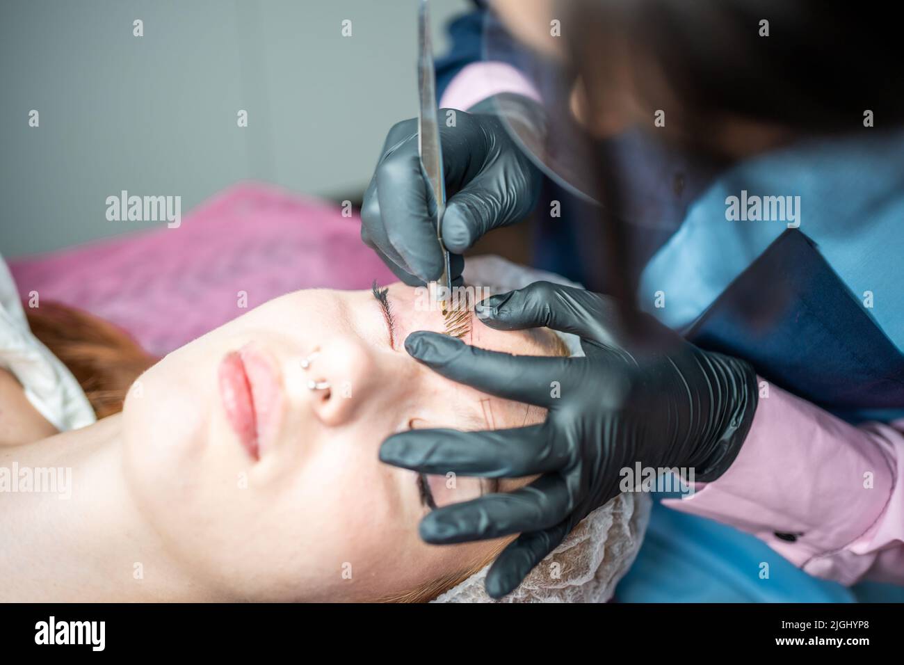 Procedure of eyebrow microblading. A master in black gloves is doing a ...