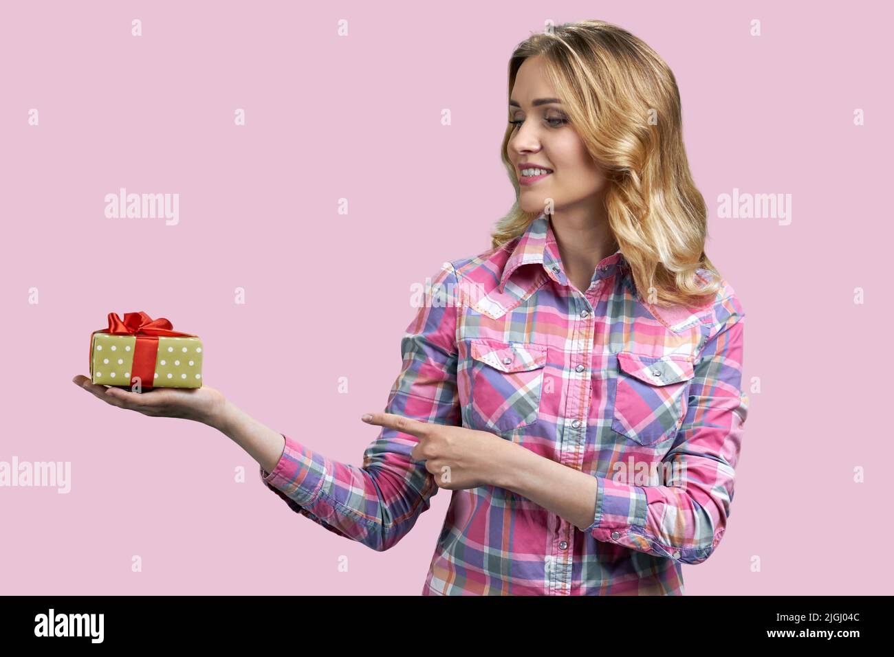 Pretty girl in stylish shirt pointing with finger at gift box in her ...