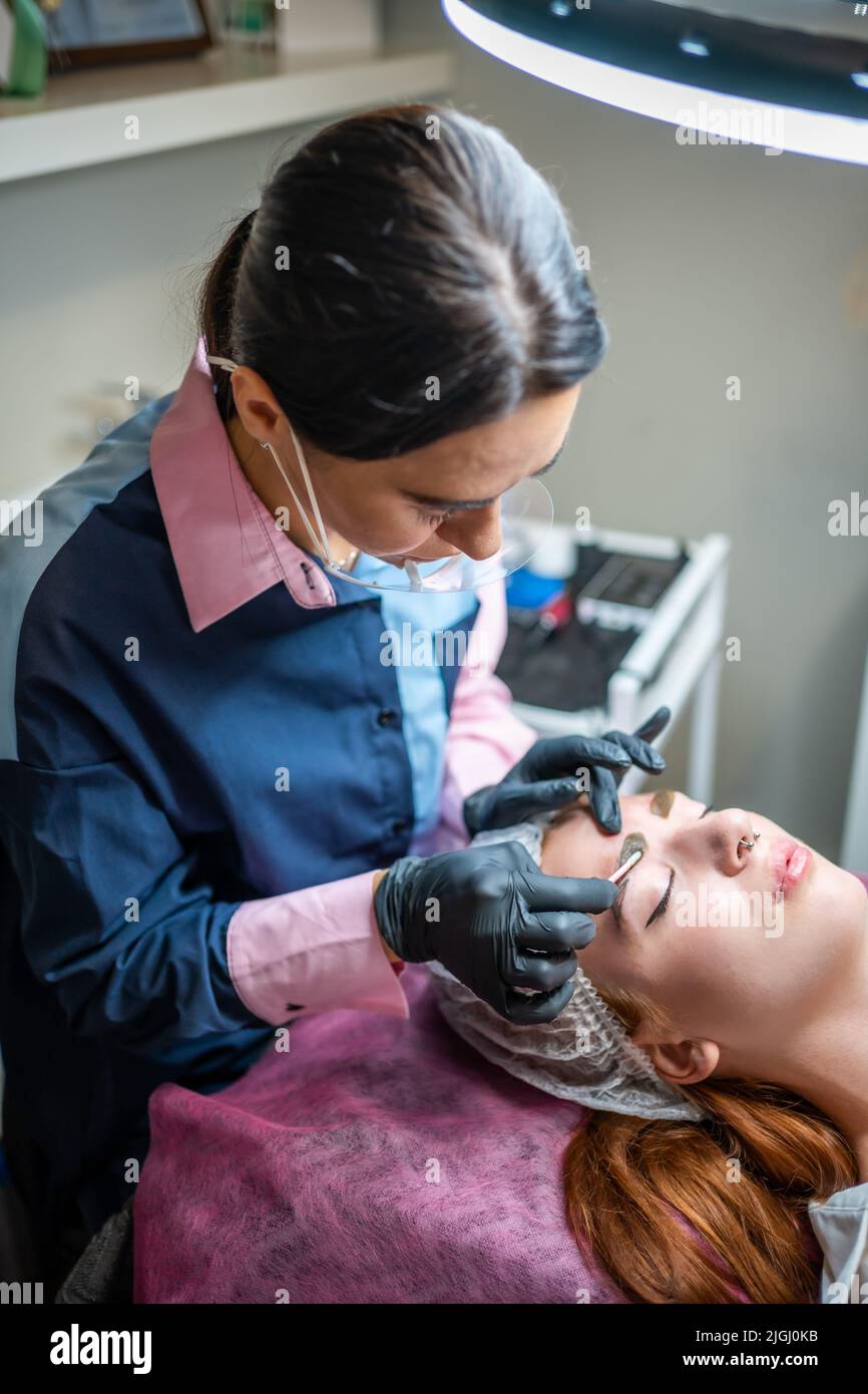 Procedure of eyebrow microblading. A master in black gloves is doing a ...