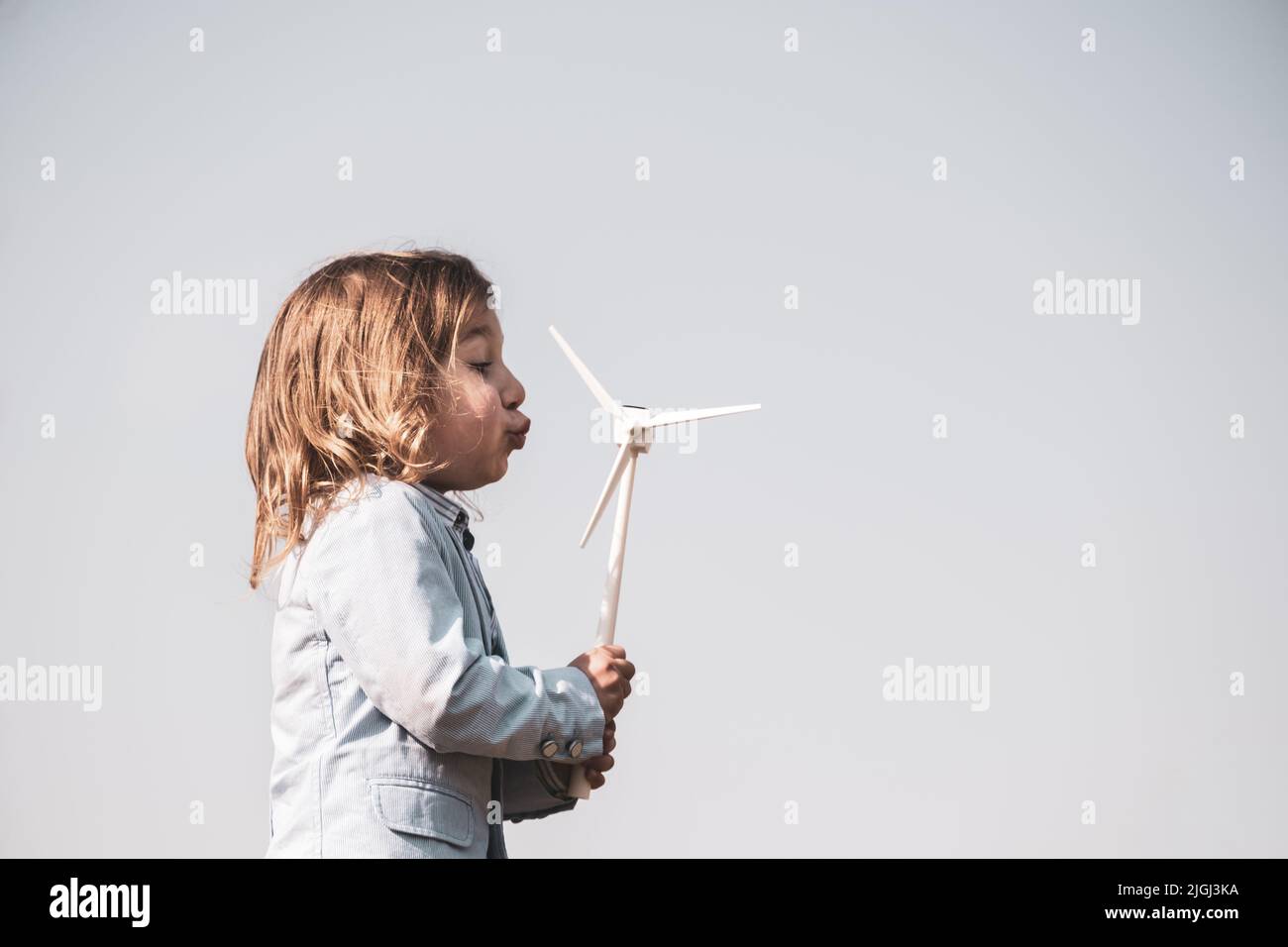 Closeup of little boy blowing a wind turbine toy and studying how green ...
