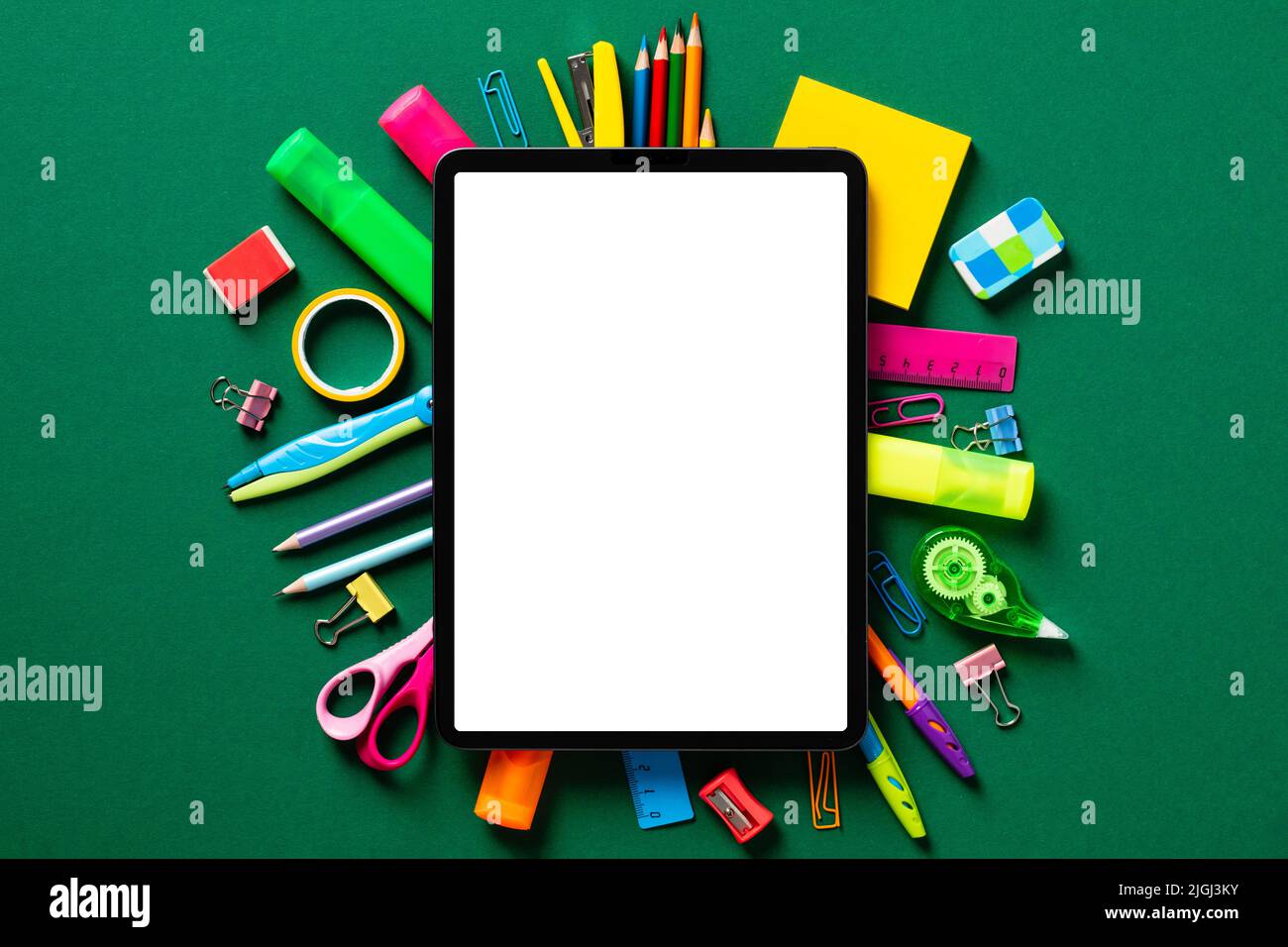 Digital tablet with colorful school supplies on green background. Back ...