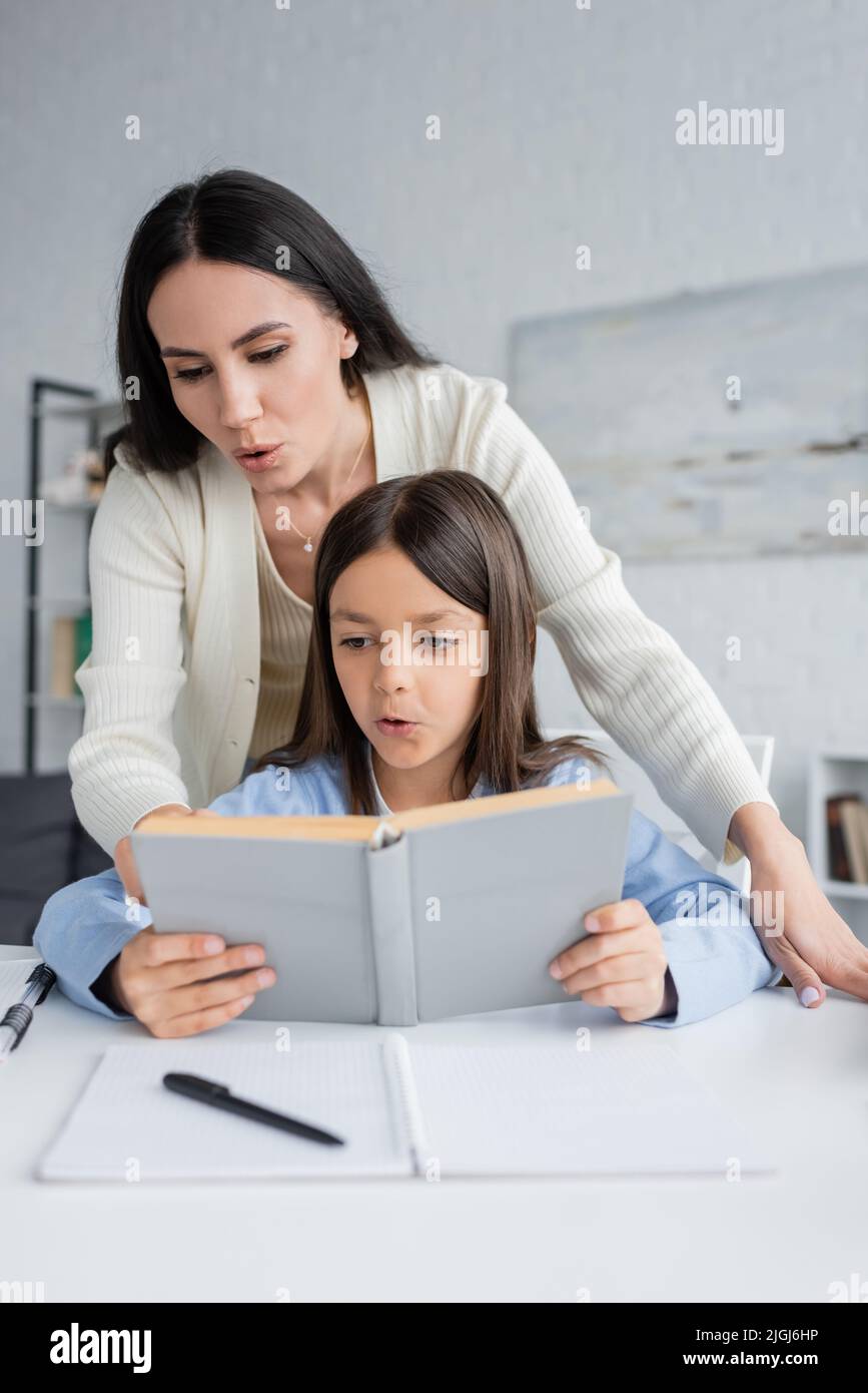 brunette nanny helping girl reading book while doing homework Stock ...