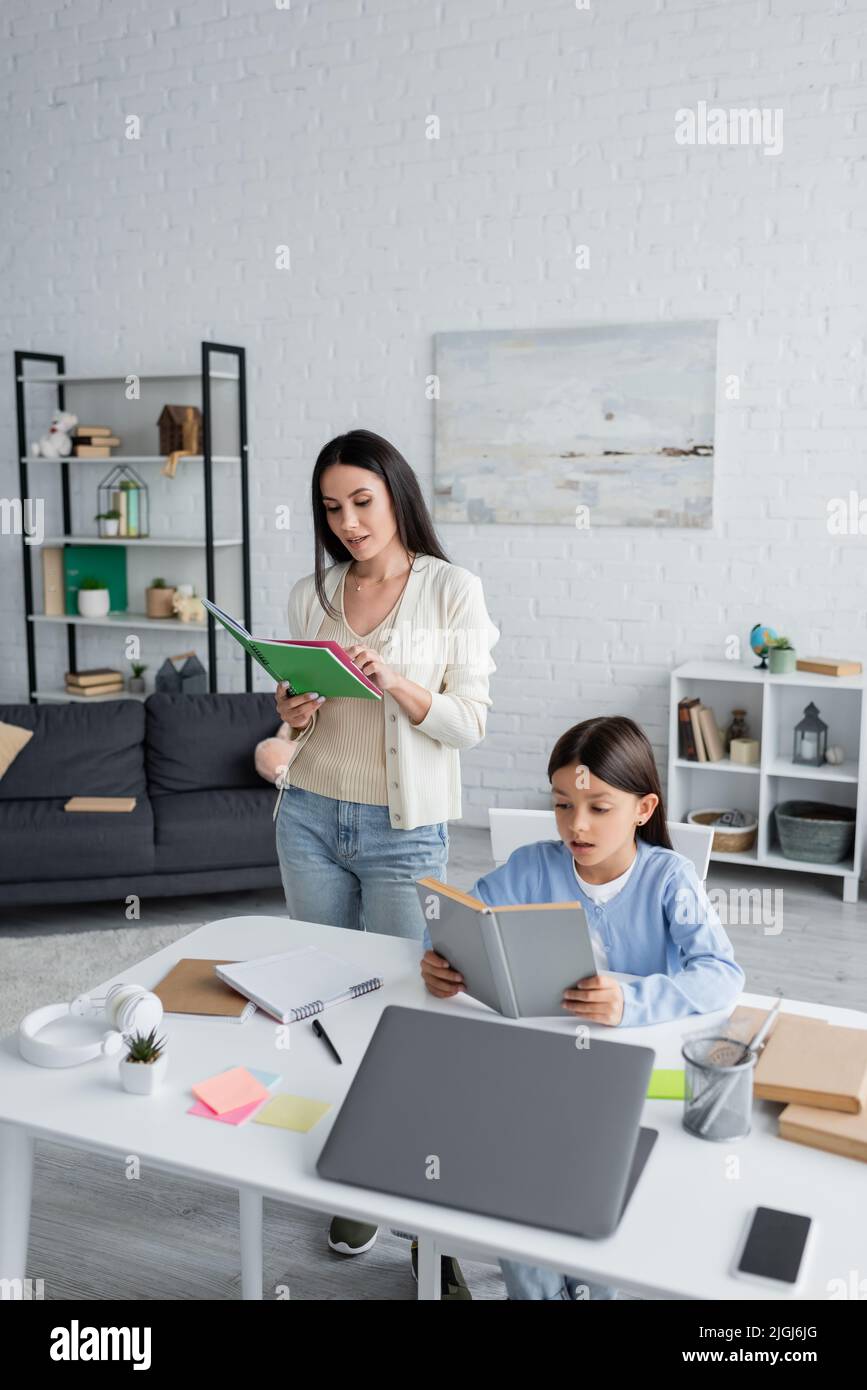 child reading book while doing homework near laptop and babysitter ...