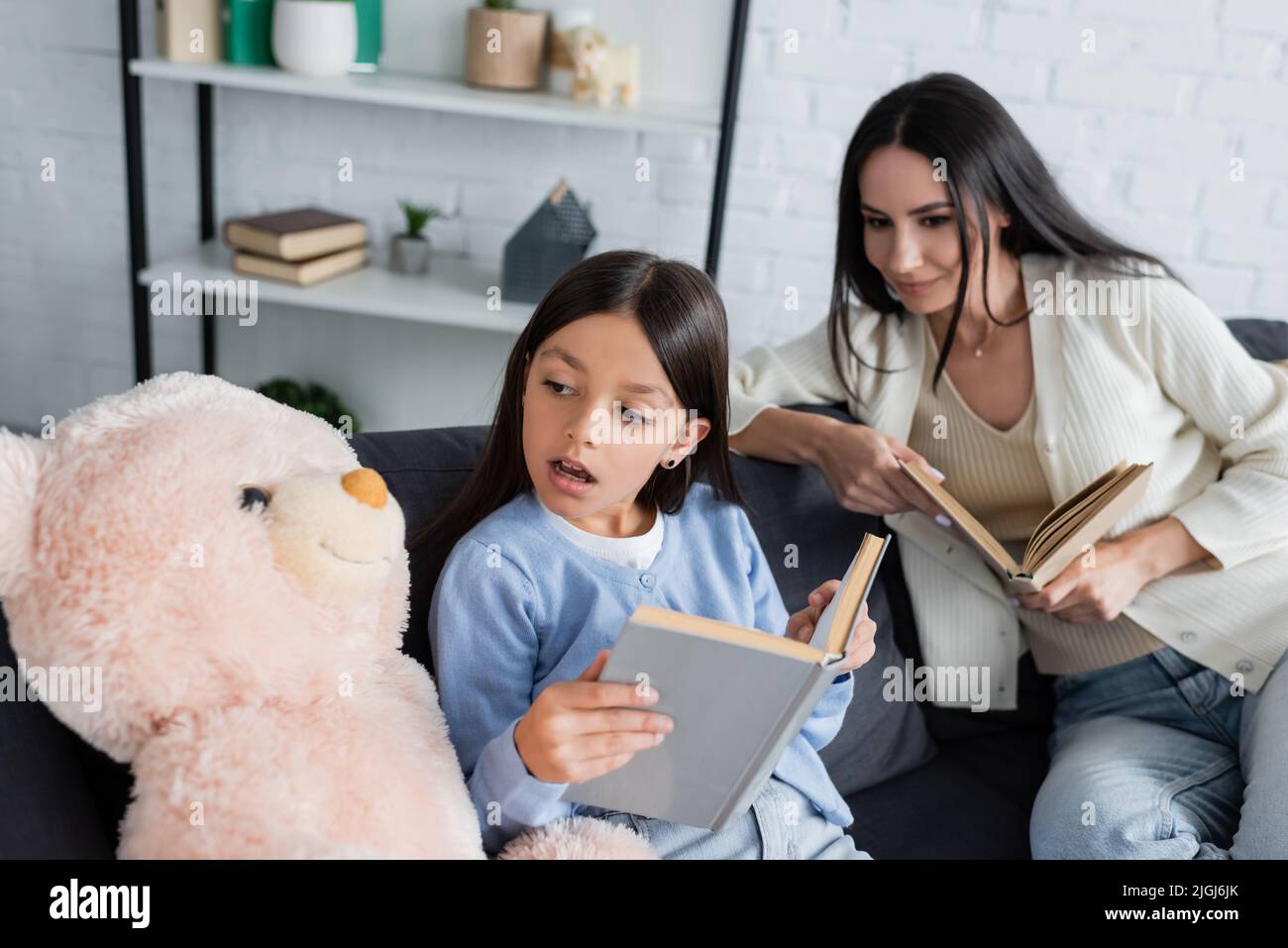 kid reading book to soft toy near smiling babysitter at home Stock ...