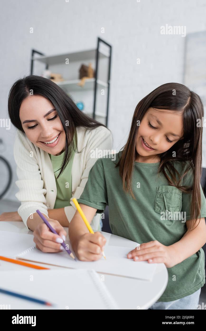 happy babysitter and cheerful kid drawing on paper with colorful ...