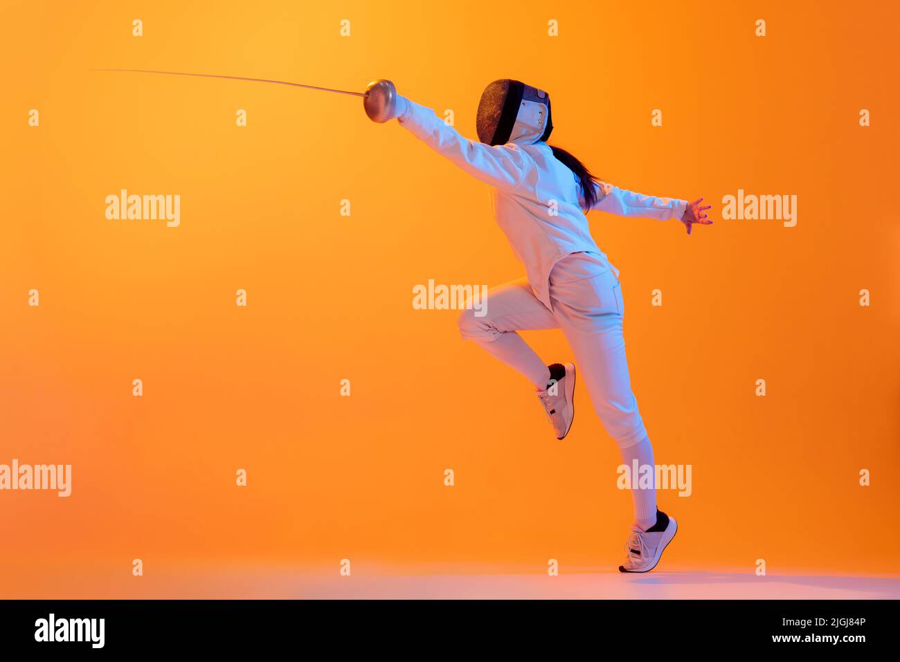 Studio shot of professional fencer in white fencing costume and mask in ...