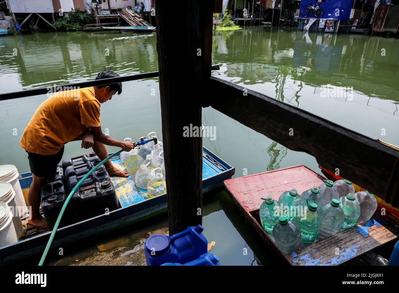 A man collects water using plastic containers at a small dock inside ...