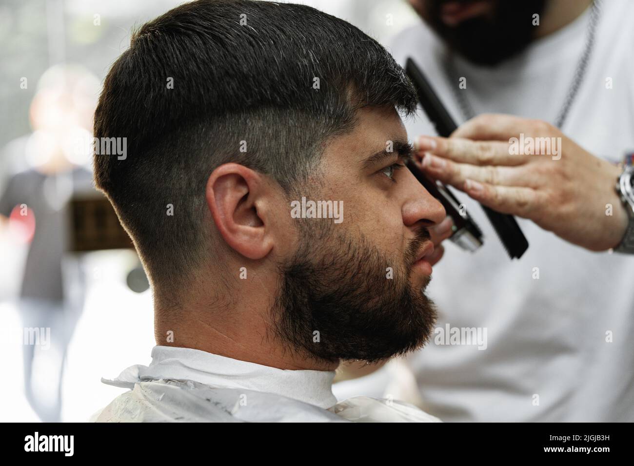 Barber guy gives a haircut to a bearded man sitting in a chair in a ...