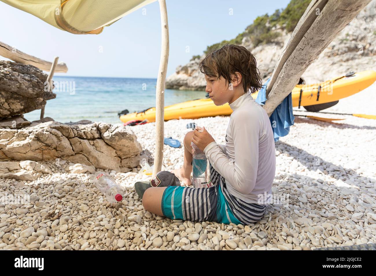 Boy sitting in a shadow on a remote beach in Kornati archipelago ...