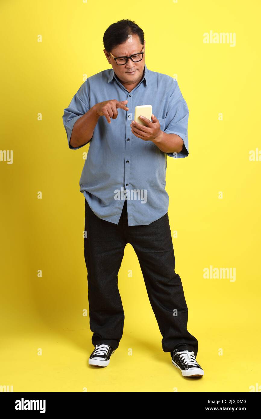 The adult Asian man with blue shirt standing on the yellow background ...