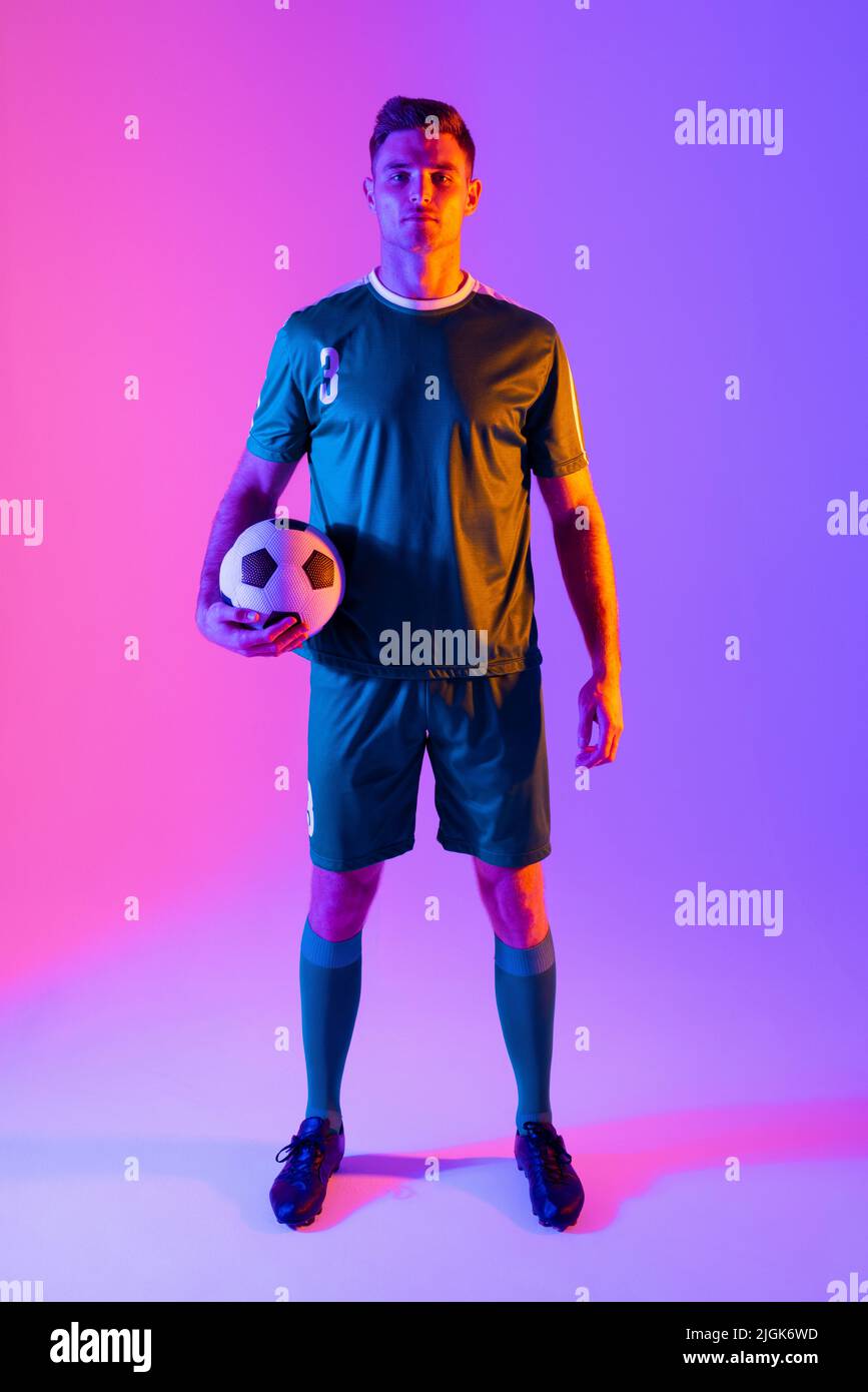 Portrait of caucasian male soccer player with football over neon pink ...