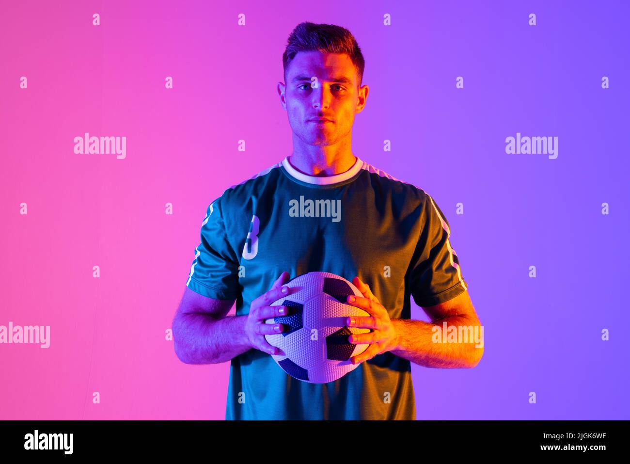 Portrait of caucasian male soccer player with football over neon pink ...