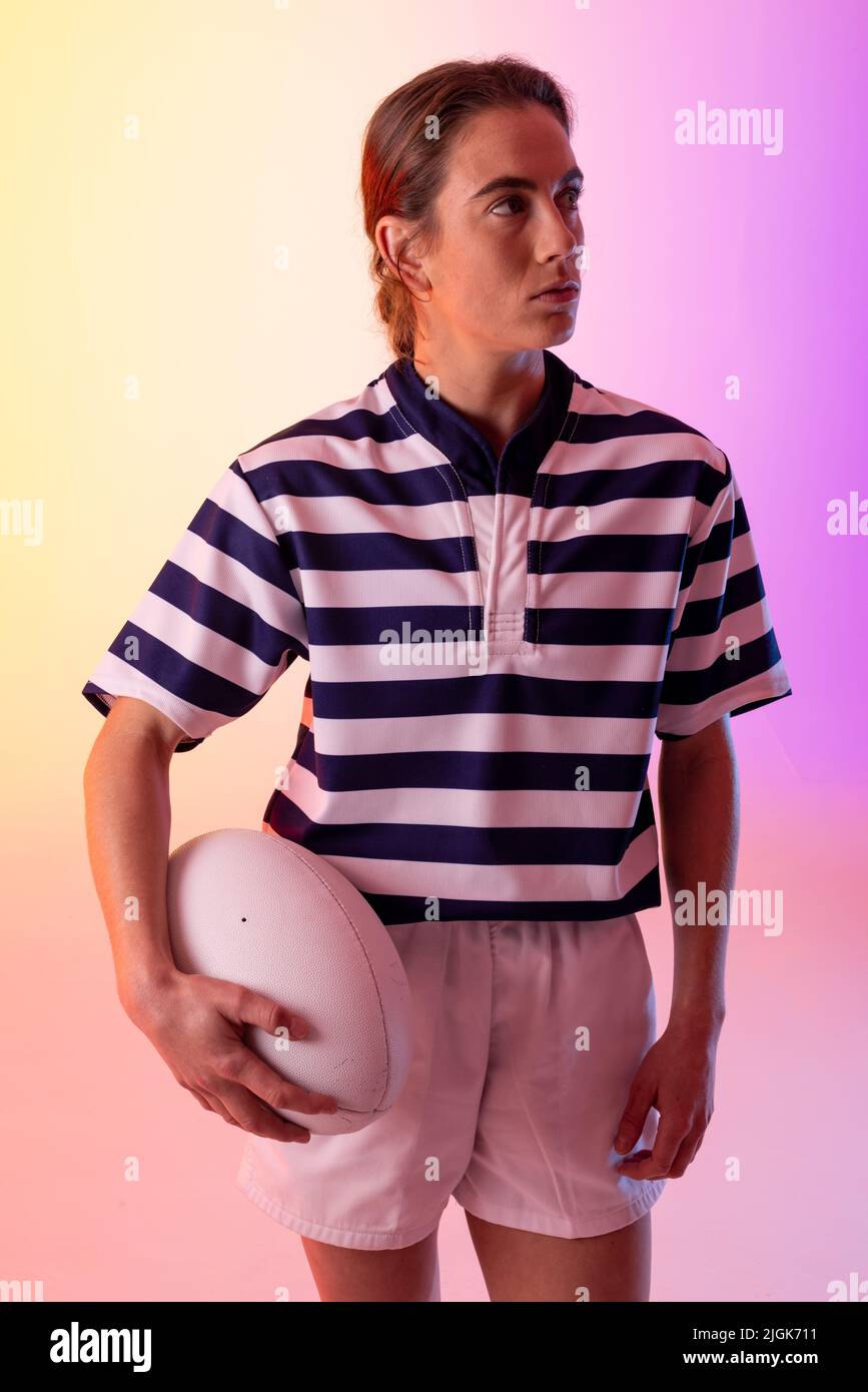 Caucasian female rugby player with rugby ball over neon pink lighting ...