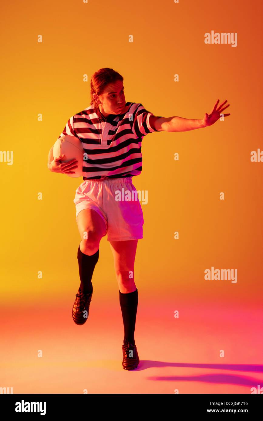 Caucasian female rugby player with rugby ball over neon pink lighting ...