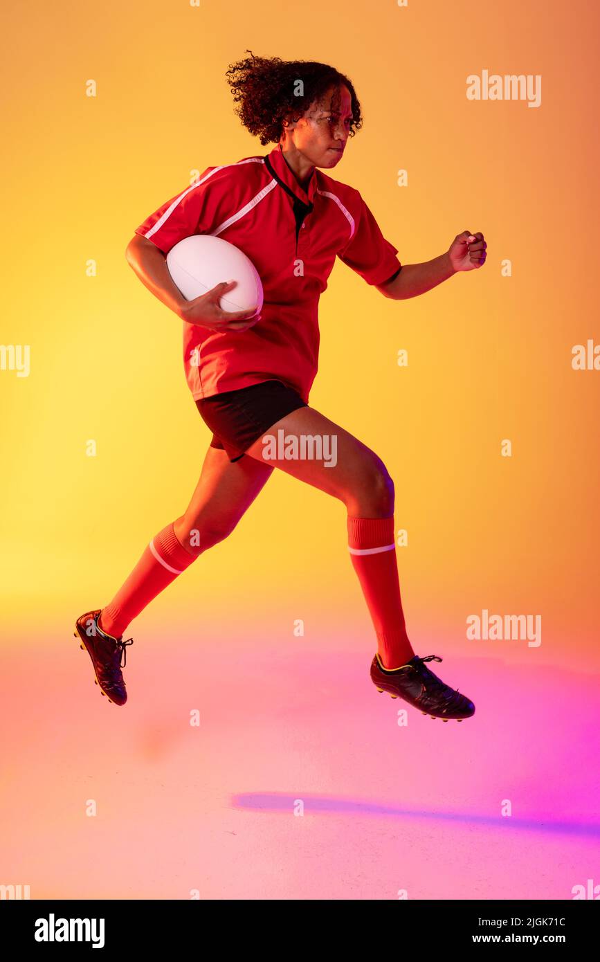 African american female rugby player running with rugby ball over neon ...