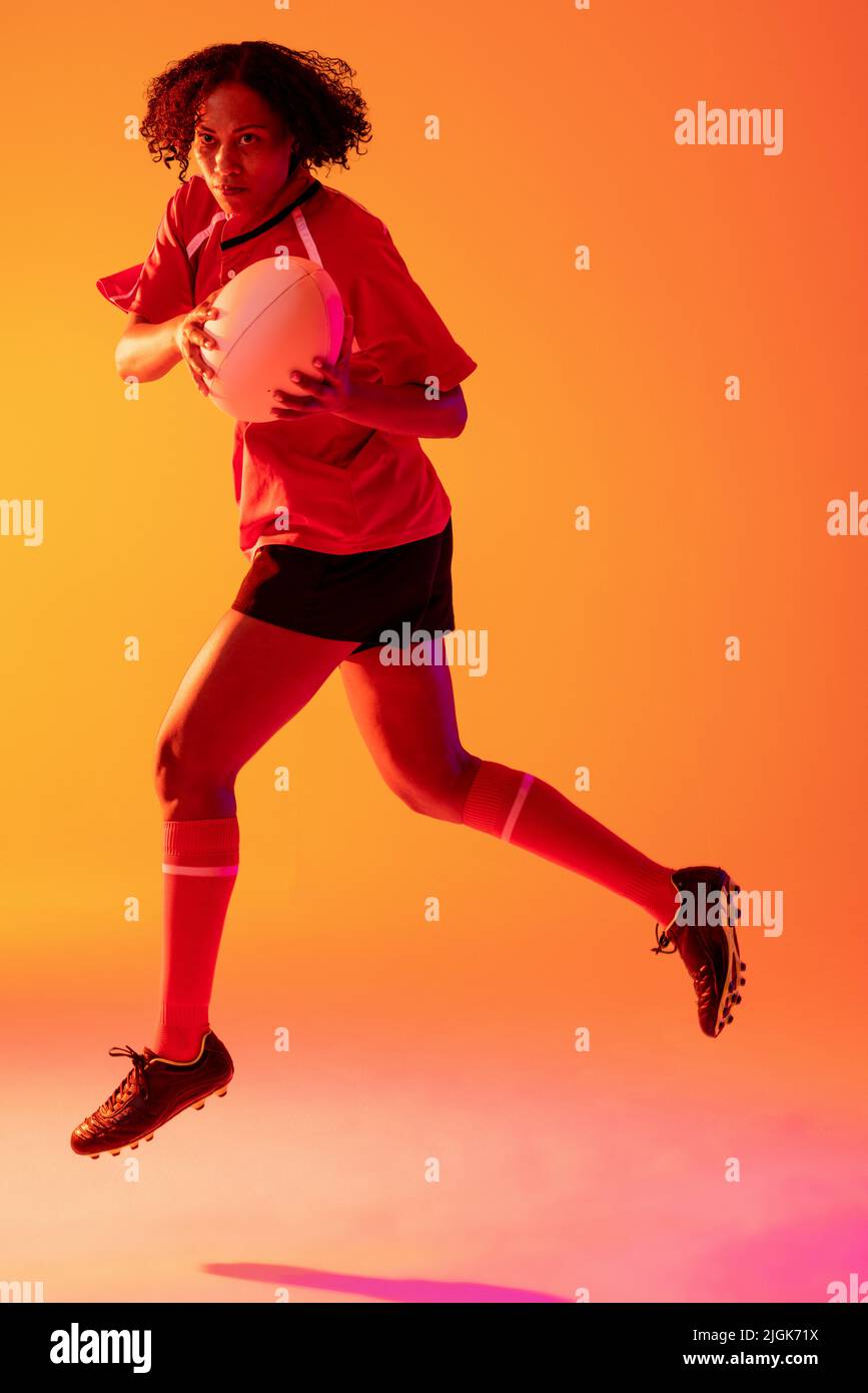 African american female rugby player with rugby ball over neon pink ...