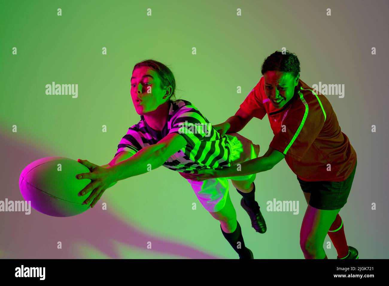 Diverse female rugby players playing rugby over neon pink lighting ...