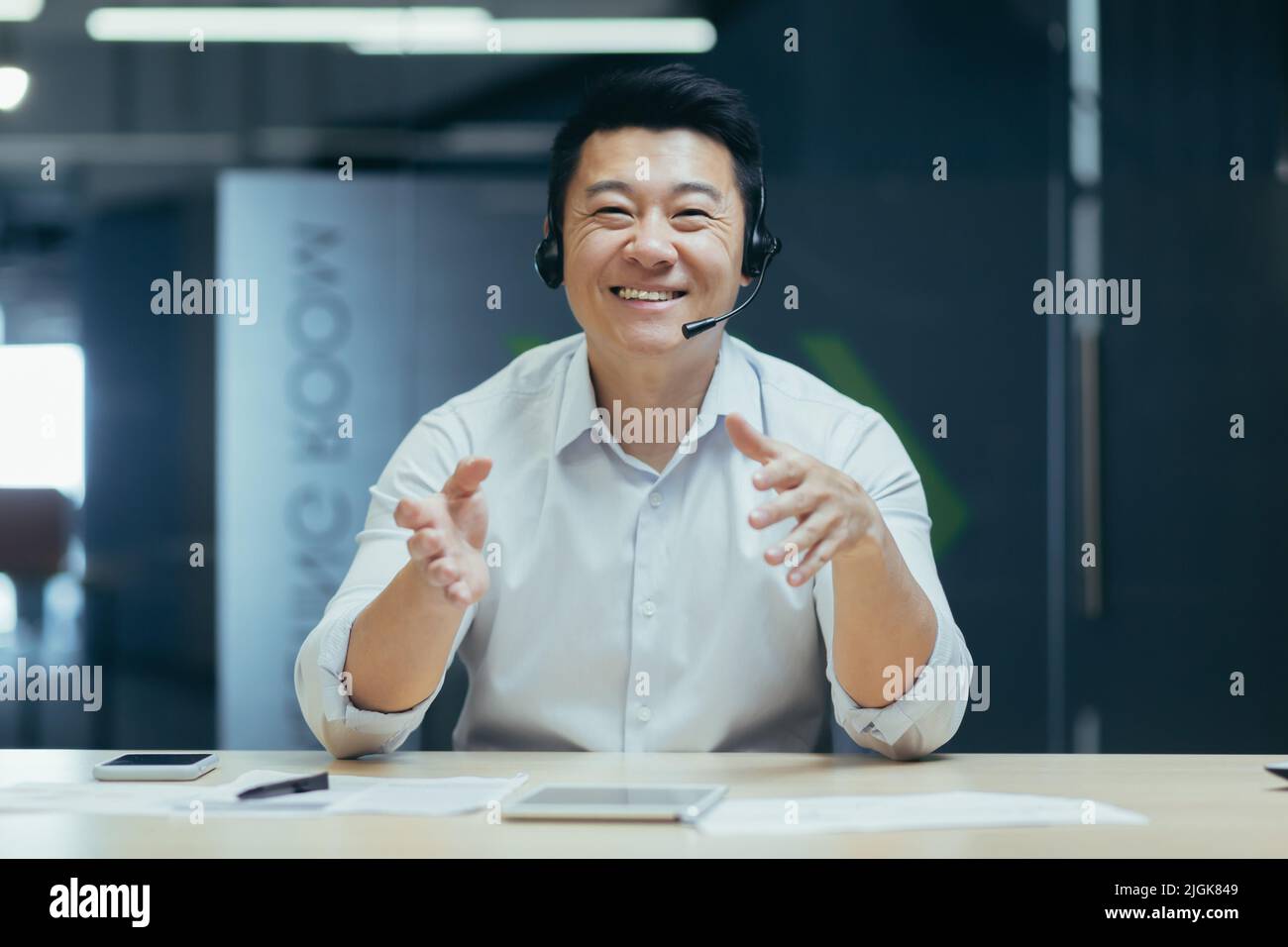 Asian man with headset talking on video call, looking into web camera ...