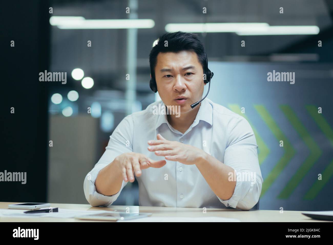 Serious and disappointed asian businessman with headset for video call ...