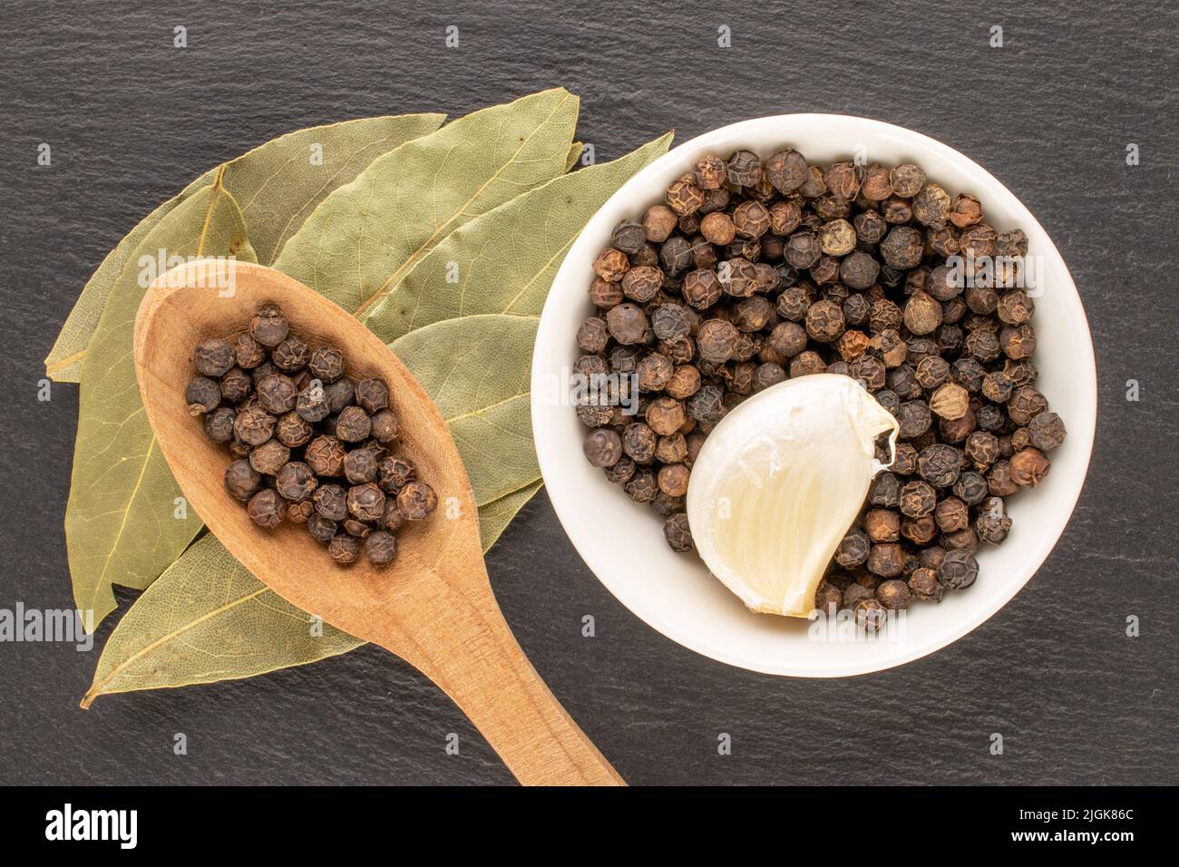 Dry fragrant black pepper in a white saucer on a slate stone, close-up ...