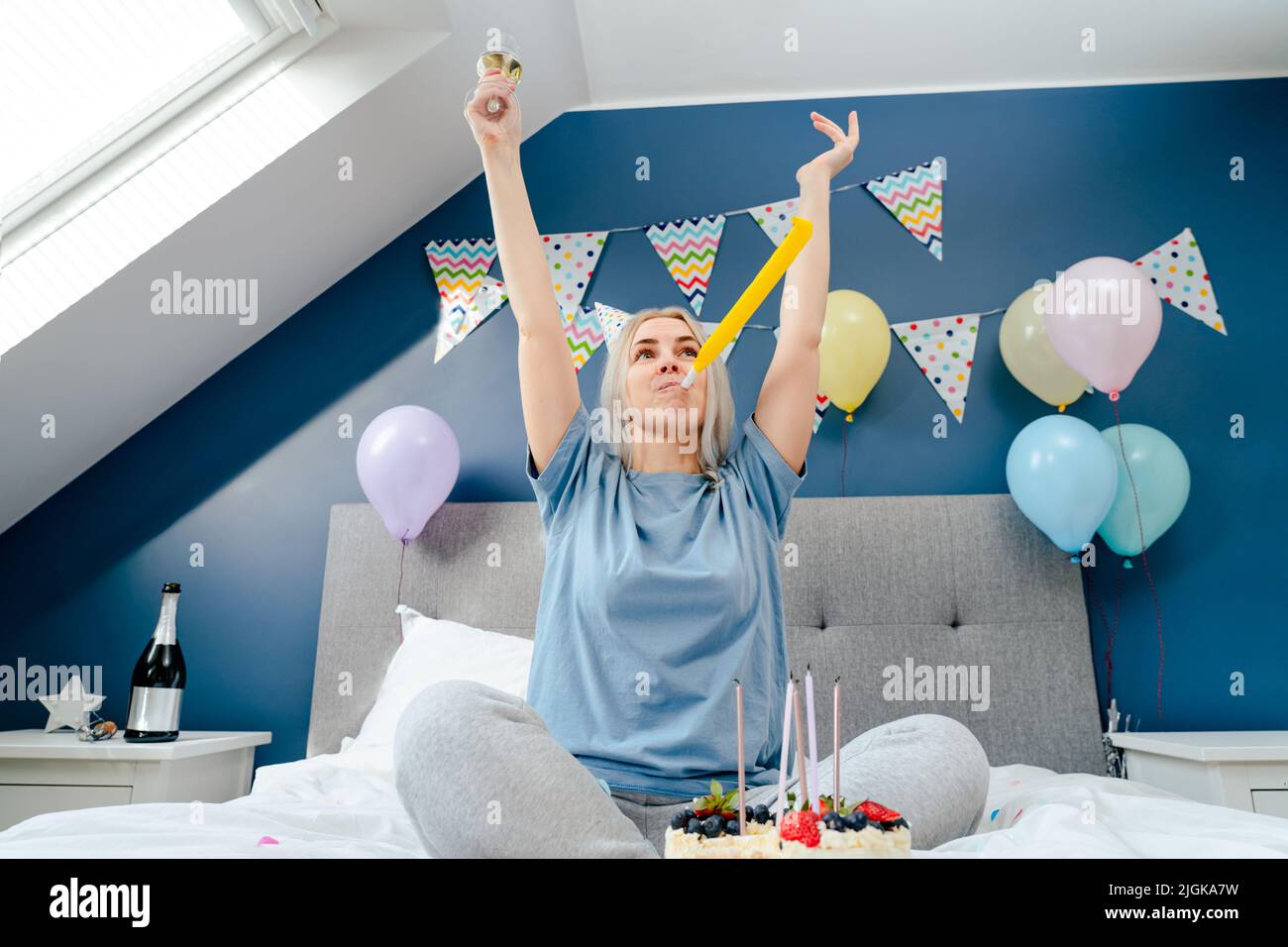 Happy emotional woman in pajama and party cap blowing in a birthday ...