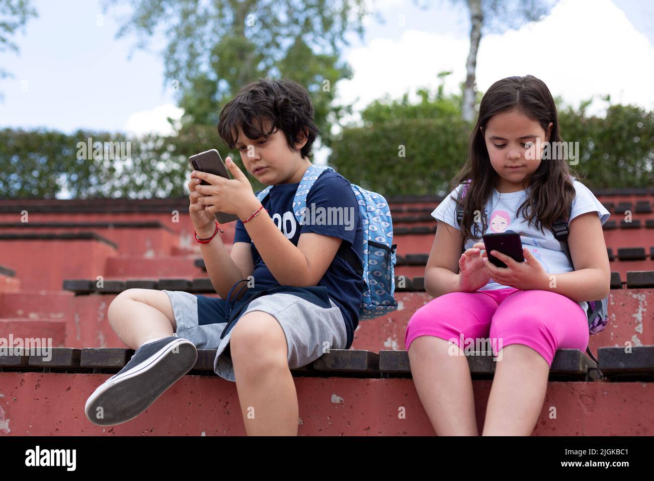 Two caucasian primary school students using mobile phones outdoors ...