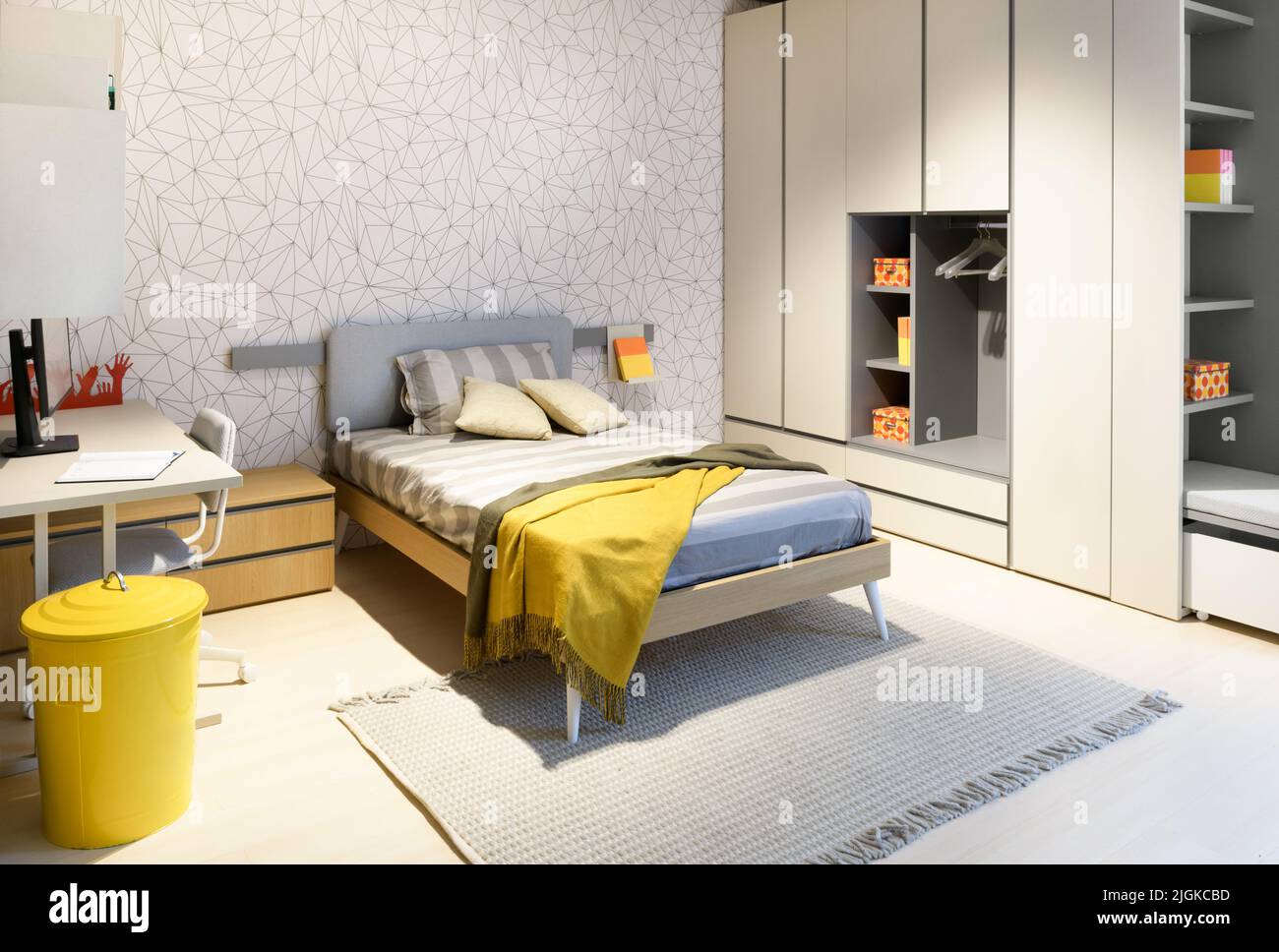 Unmade comfortable bed located between desk with computer and wardrobe ...