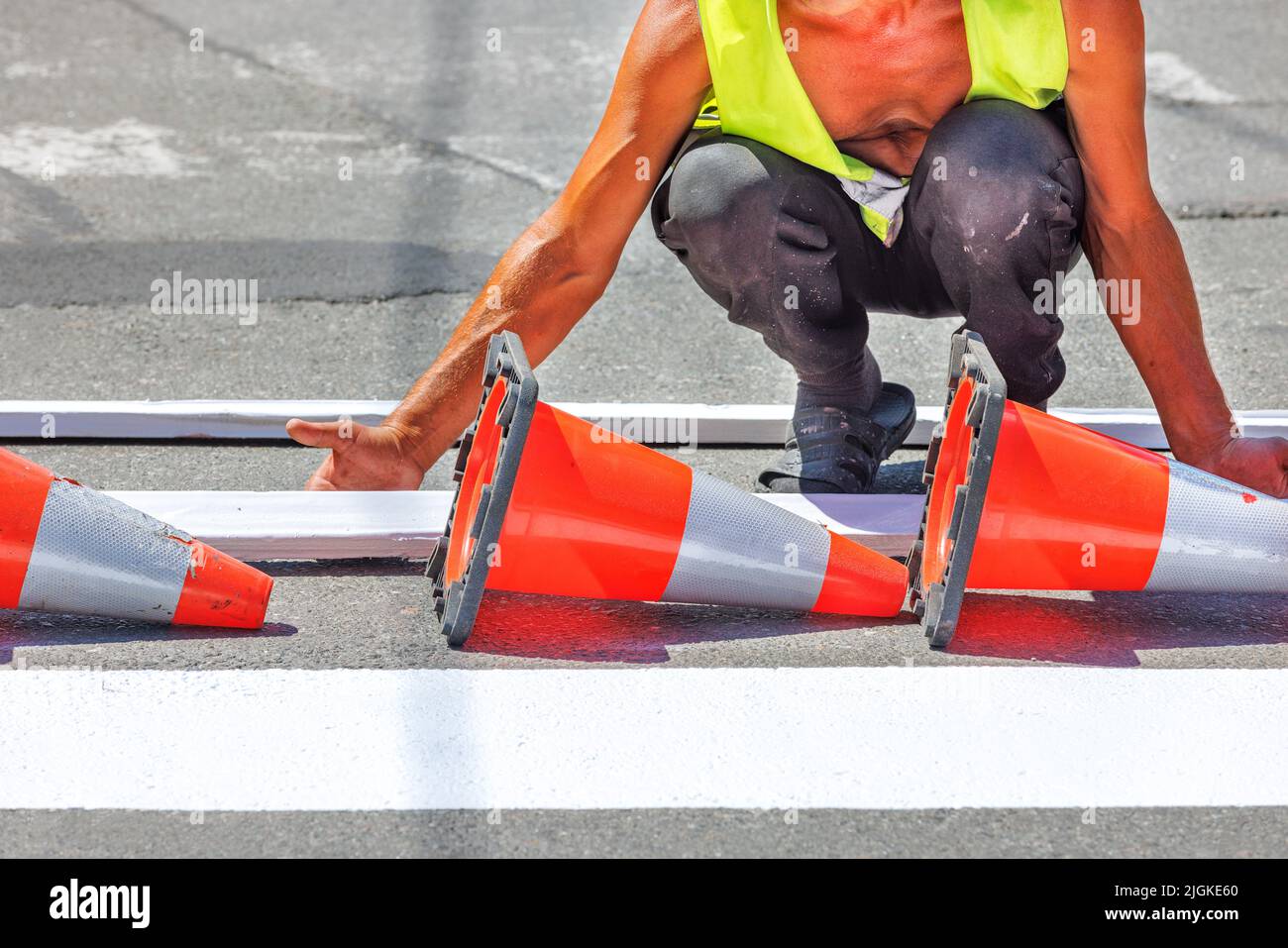 A road worker applies white road markings to a pedestrian crossing ...
