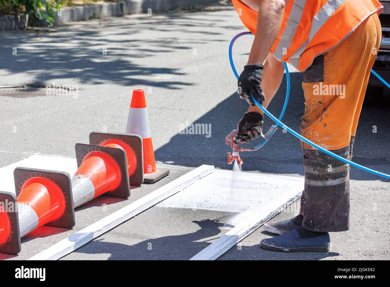 A road worker using a paint sprayer applies white road markings to a ...