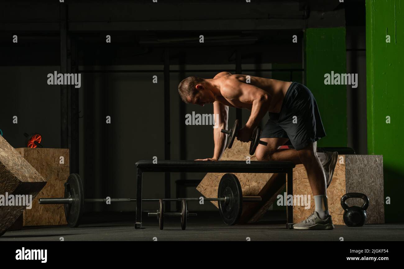 Good looking young man doing triceps dumbbell kickback exercises with ...
