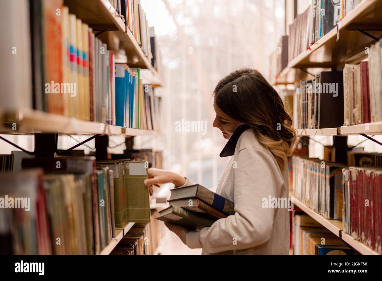 College girl talking on the phone while putting back a book Stock Photo ...