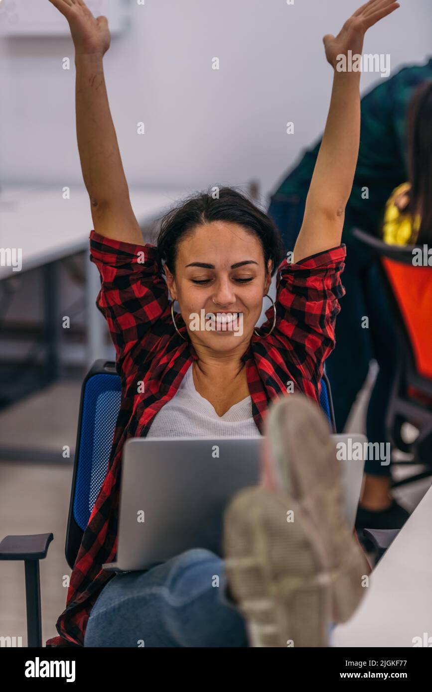 A young female worker with her hands up in the air, her legs on the ...