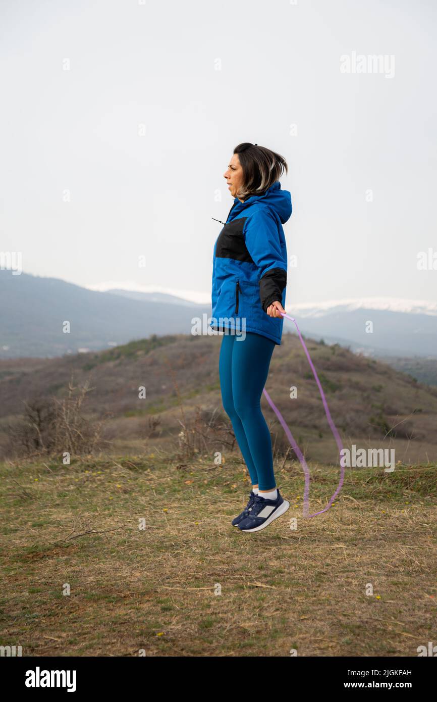 Amazing and active woman is doing a jumping rope exercise in the forest ...