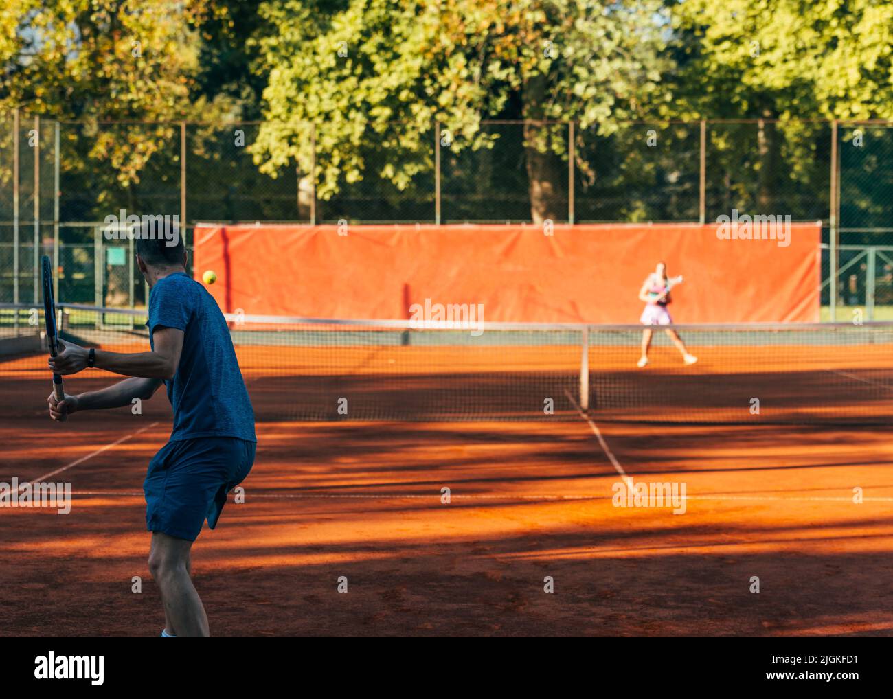 Rearview of a tennis player ready to serve on a clay court wearing blue ...