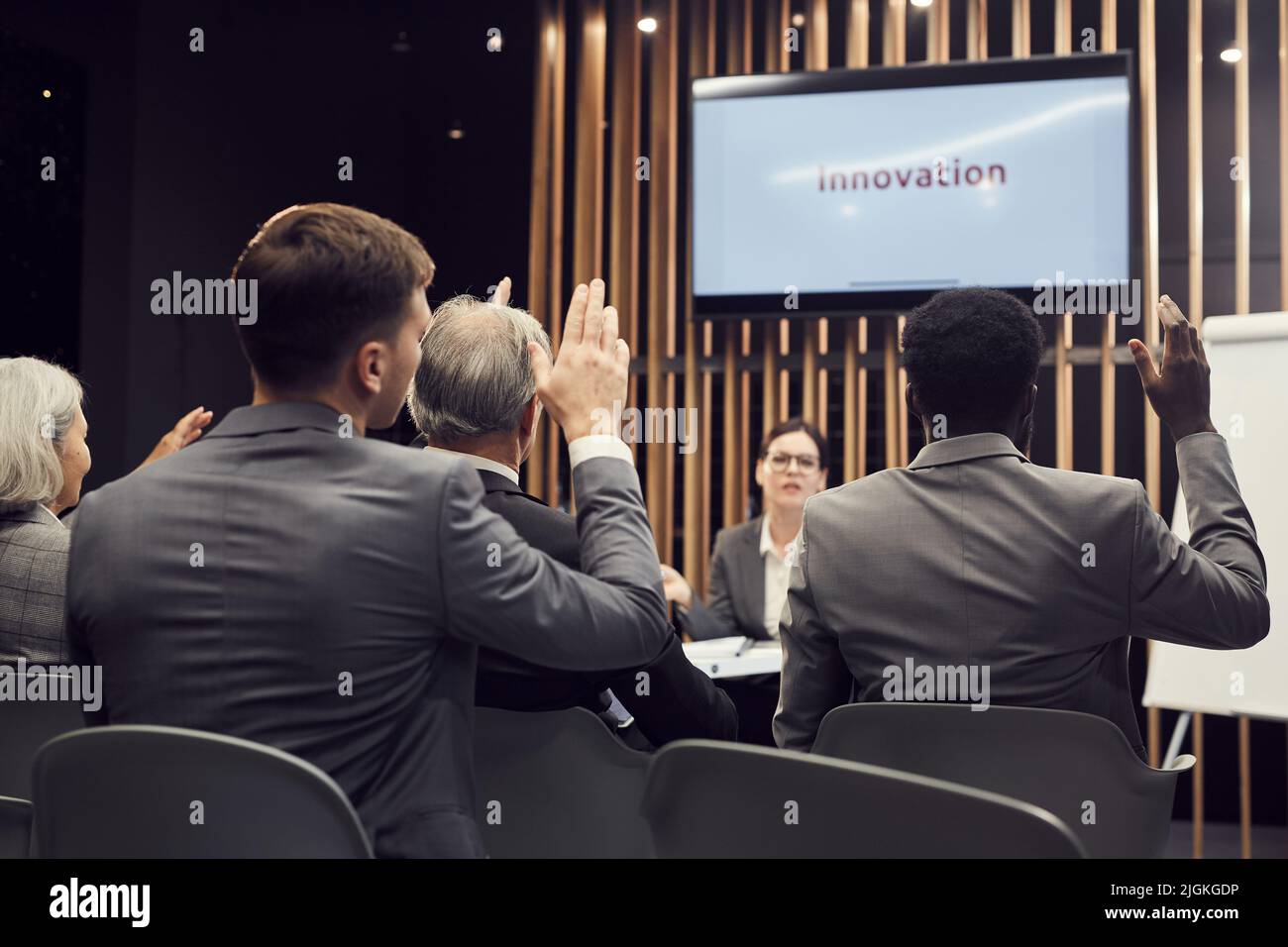 Rear view of business participants raising hands while asking questions ...