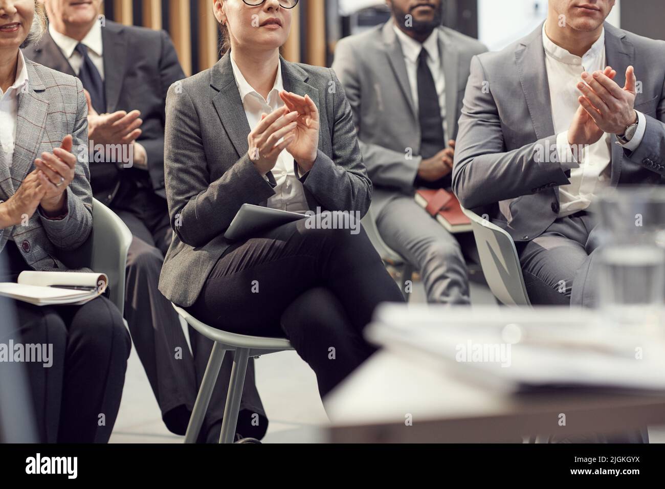 Close-up of business audience sitting on chairs and clapping hands to ...