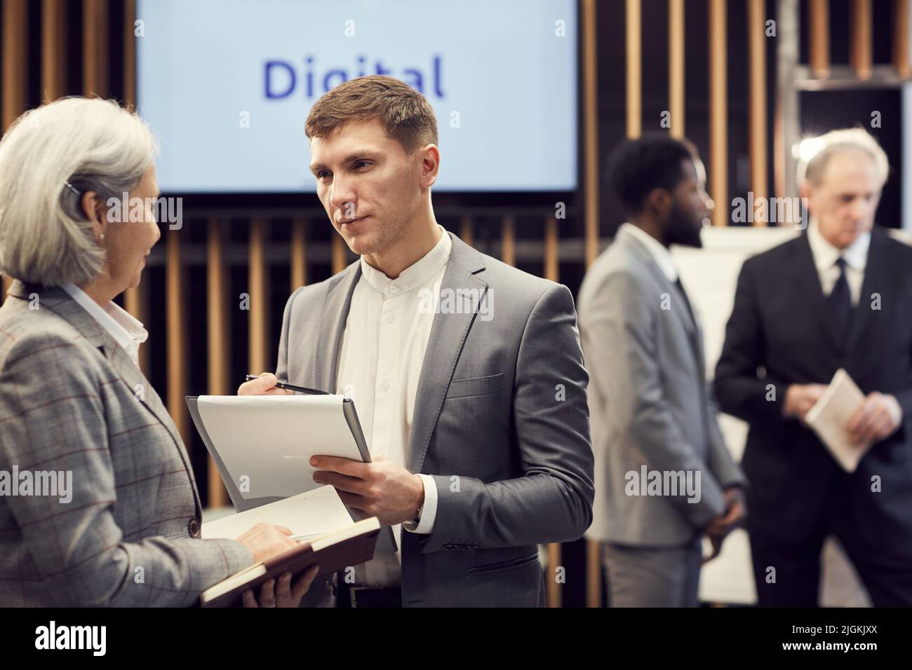 Serious handsome young journalist in suit making notes in clipboard ...