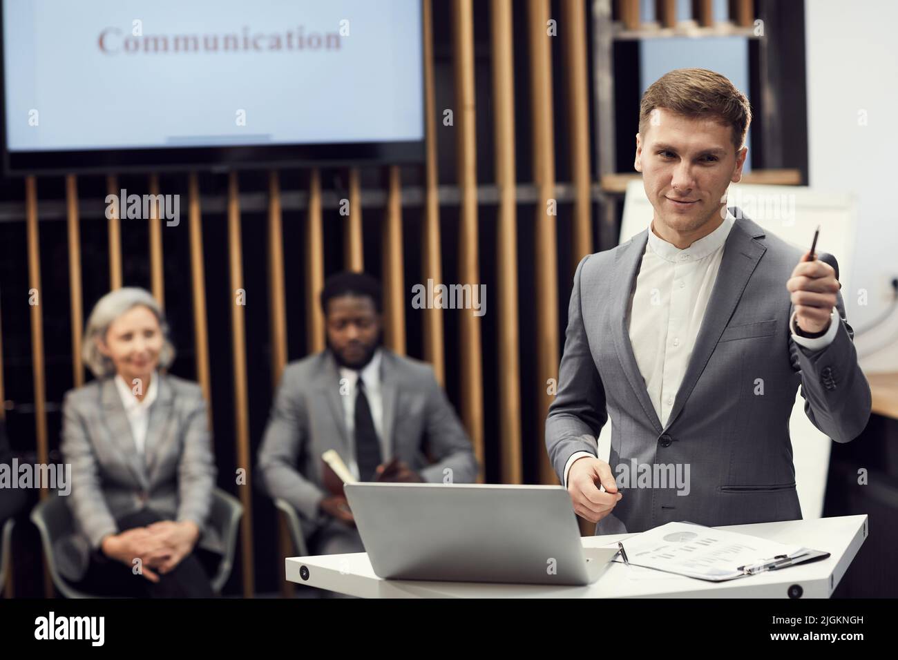 Content handsome young manager in gray suit standing at speech table ...